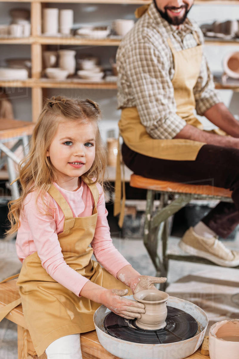 Kid making ceramic pot on pottery wheel with teacher in workshop ...