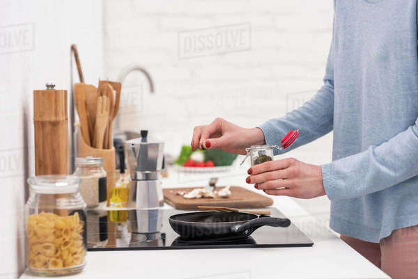 Cropped shot of woman pouring spices onto food cooking on frying pan ...