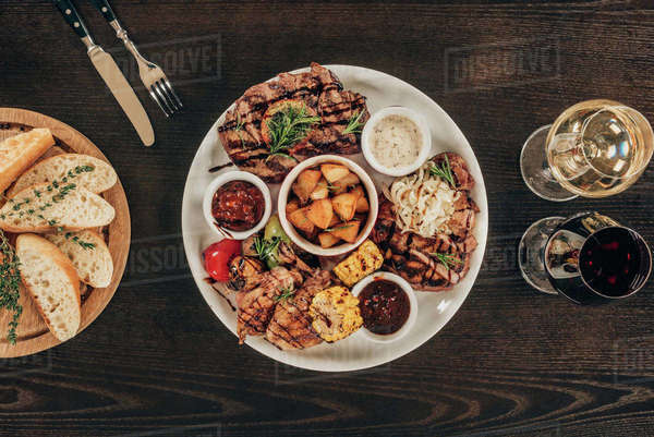 Top view of plate with beef steaks, chicken wings and wine with bread ...