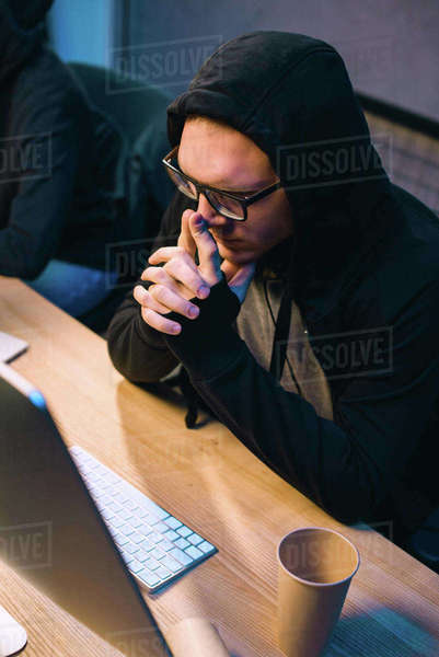 Thoughtful hooded hacker looking at computer screen - Stock Photo ...