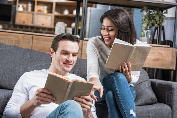 Happy multiethnic couple reading books together at home - Royalty-free ...