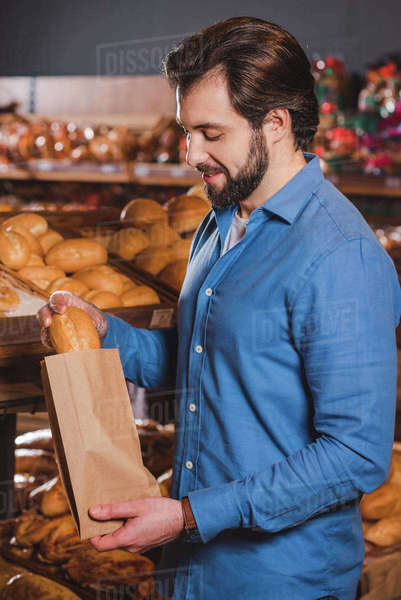 Side view of smiling man choosing bread in hypermarket - Royalty-free ...