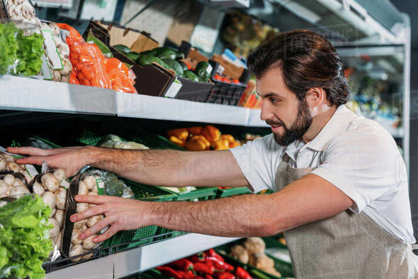 Shop assistant arranging fresh vegetables in grocery shop - Stock Photo ...