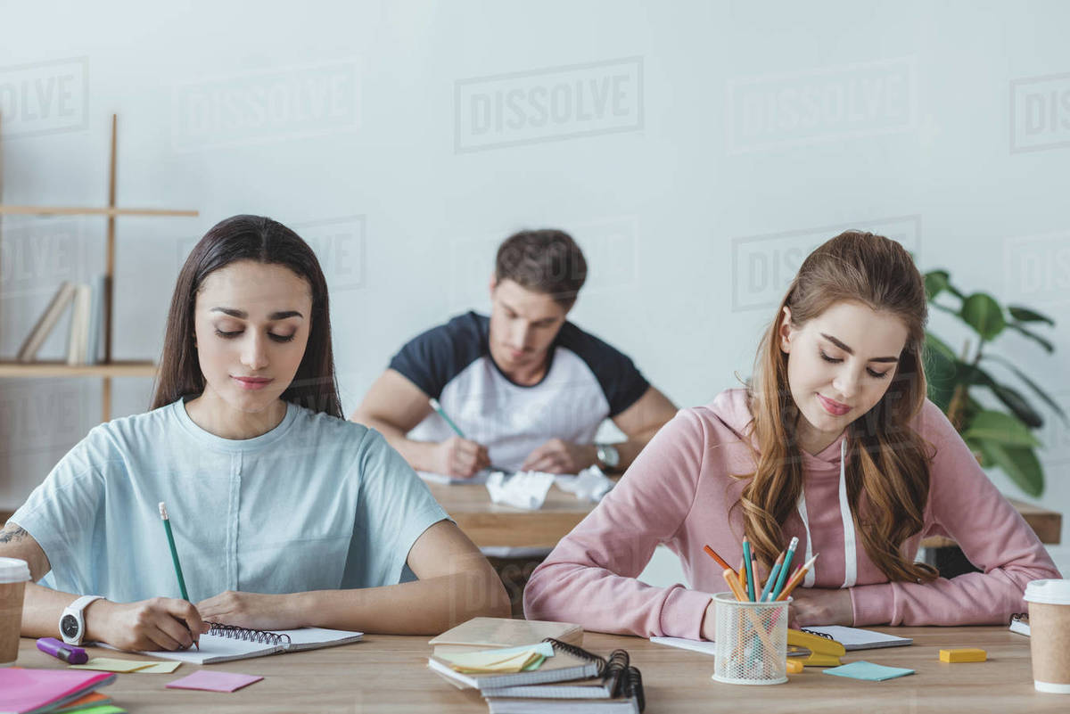 Young students sitting at tables and writing exam together - Royalty ...