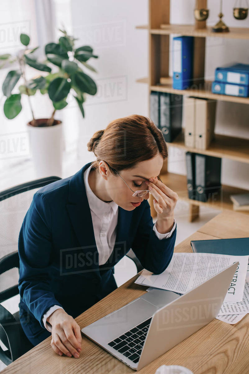 Tired female lawyer at workplace with documents and laptop in office ...