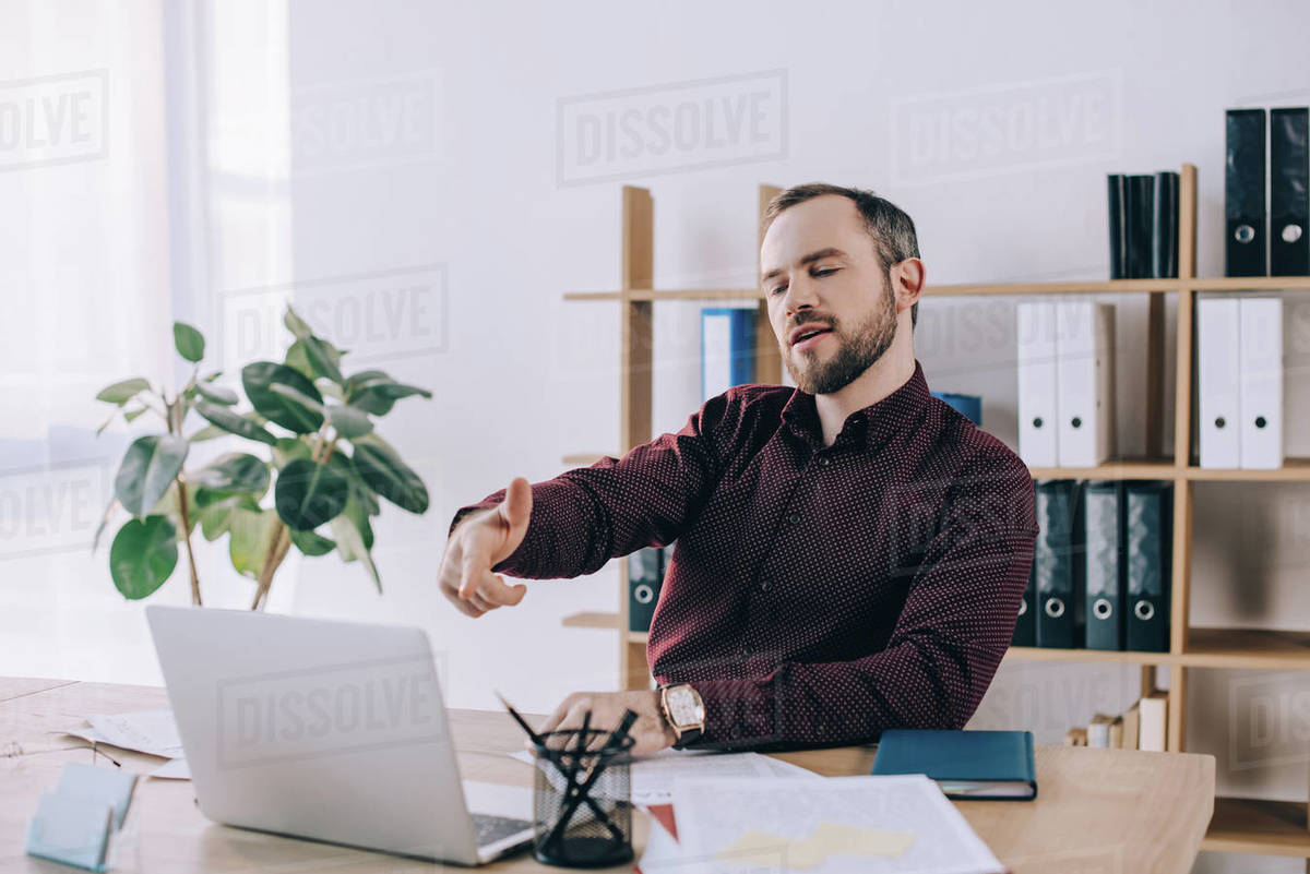 Portrait of businessman pointing at laptop screen at workplace in ...