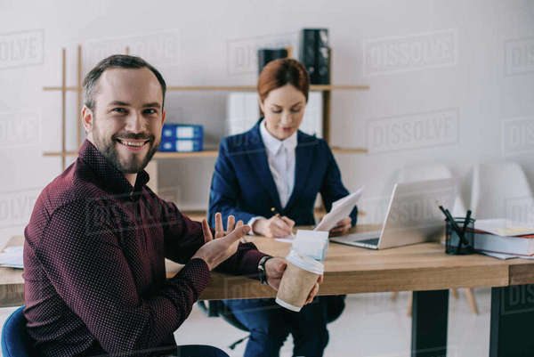 Selective focus of smiling client with coffee to go pointing at ...