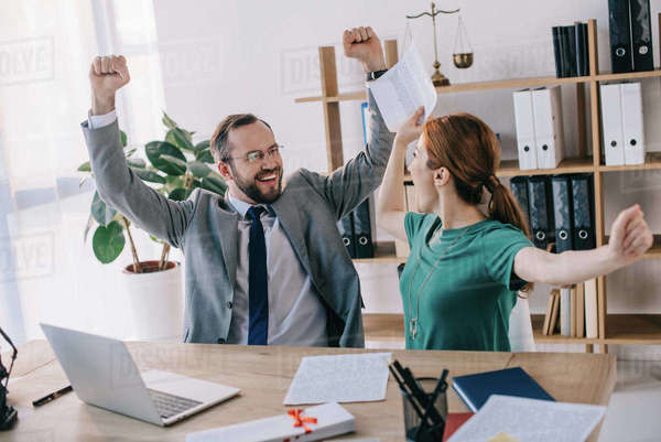 Happy lawyer and client at workplace with documents and laptop in ...