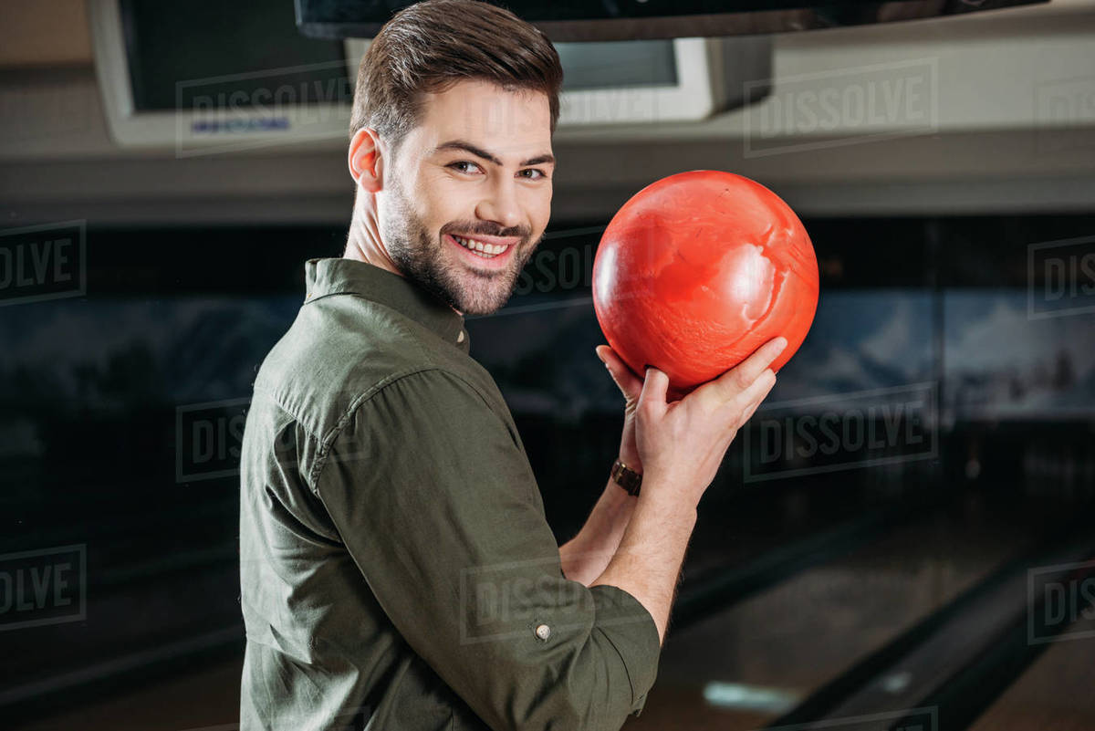 Smiling young man holding bowling ball and looking at camera - Royalty ...