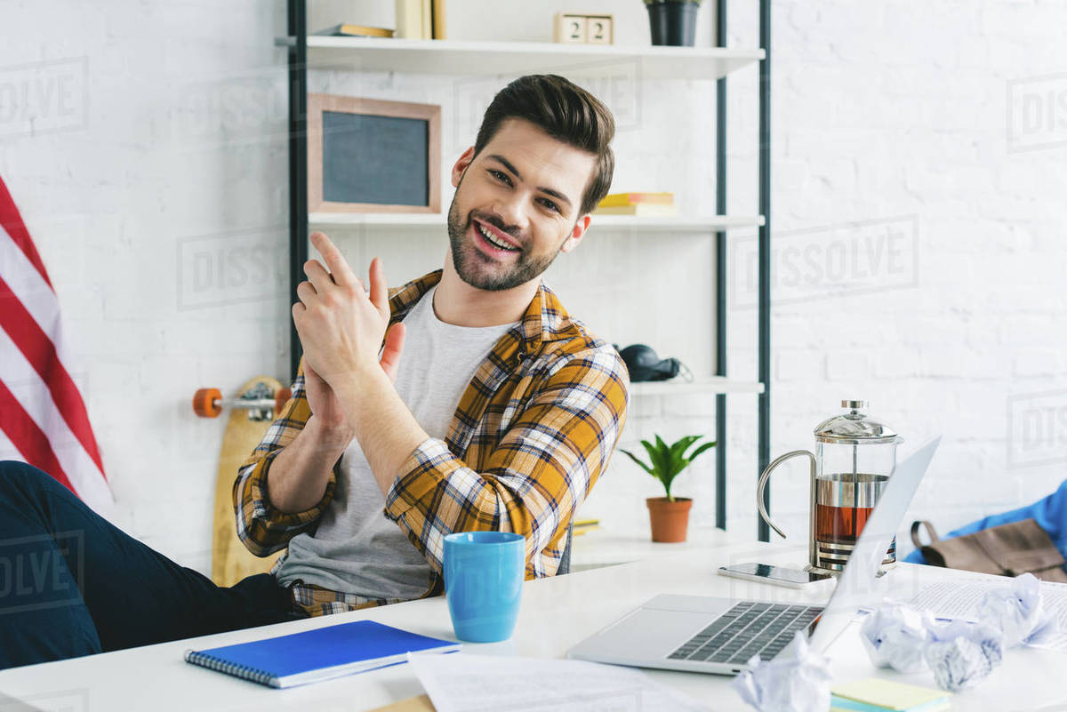 Smiling man sitting by table with laptop in light office - Royalty-free ...