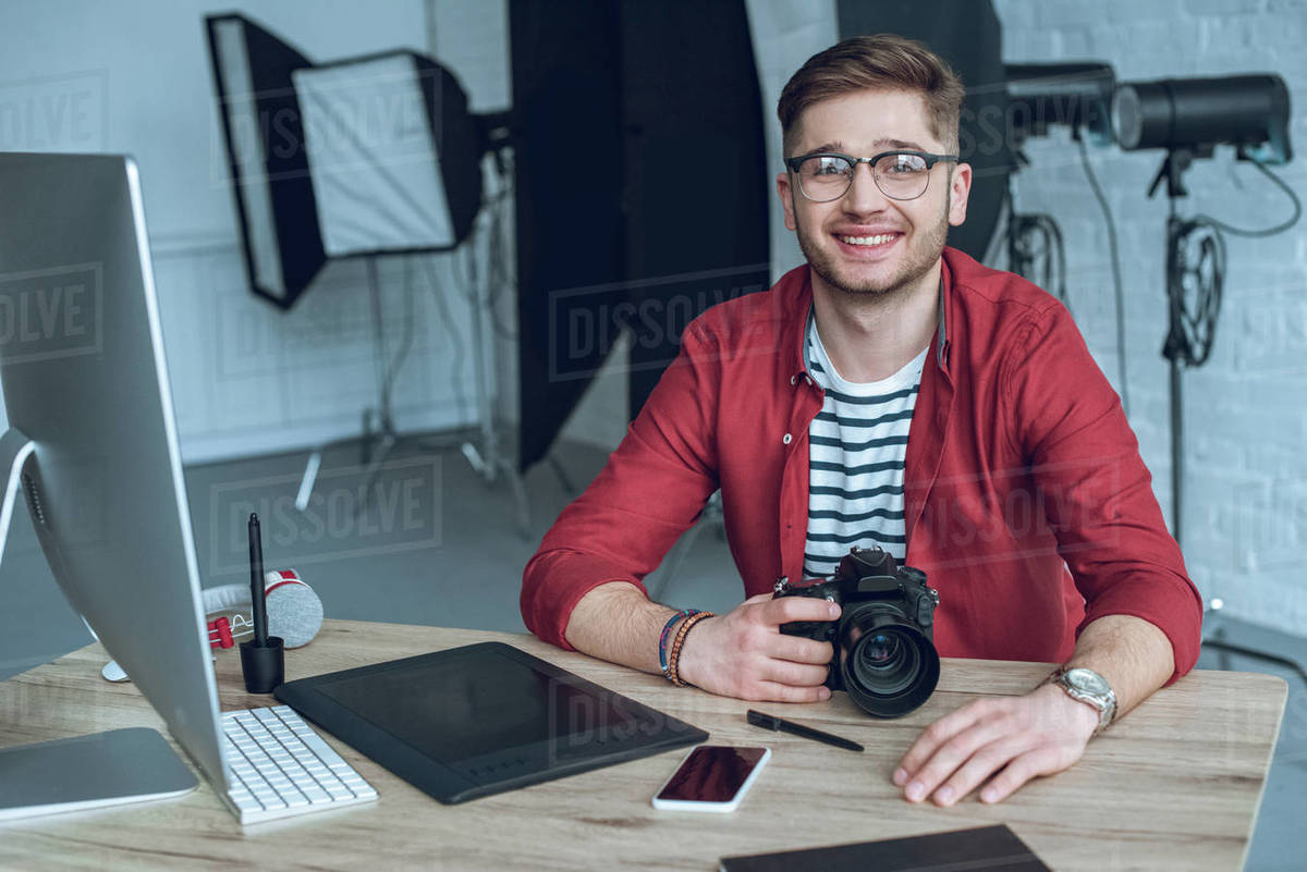 Happy freelancer man sitting by working table with camera and graphic ...