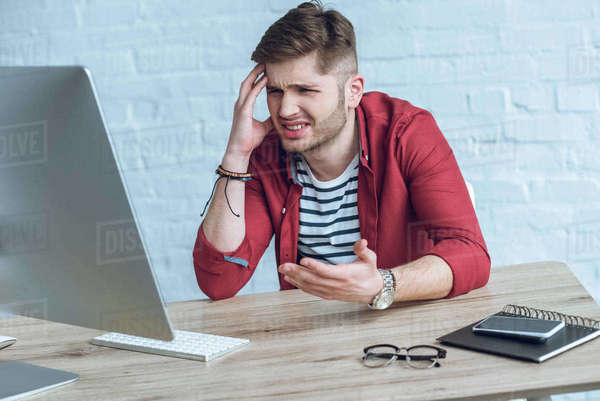Upset emotional man looking at computer screen - Stock Photo - Dissolve