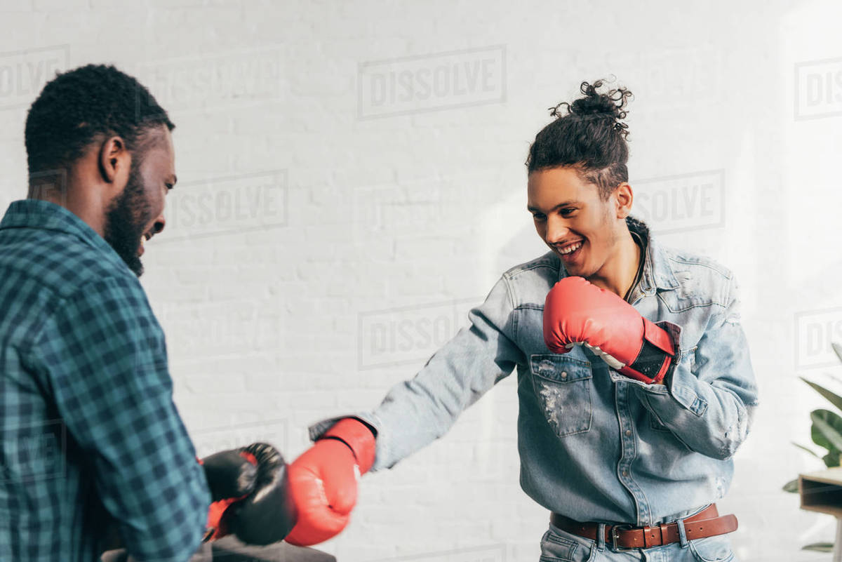 Young smiling multiethnic male friends doing sparring in boxing gloves ...