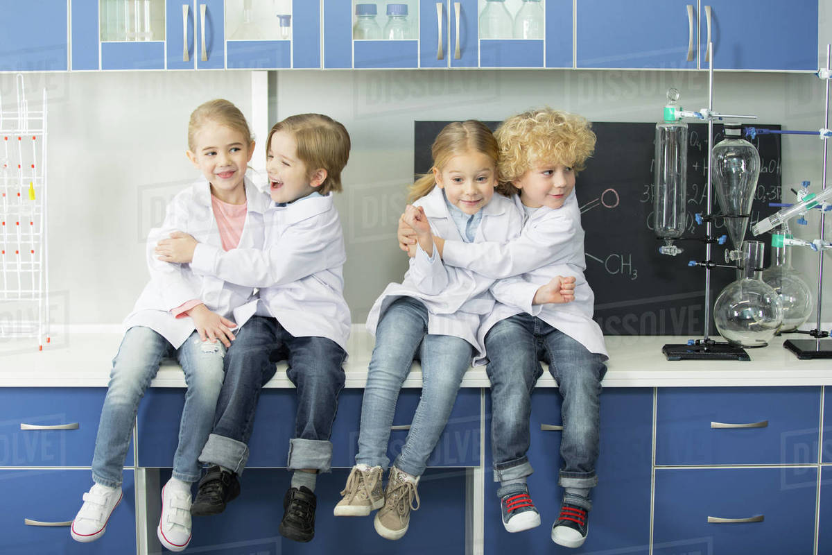 Schoolchildren in lab coats sitting together in chemical laboratory ...