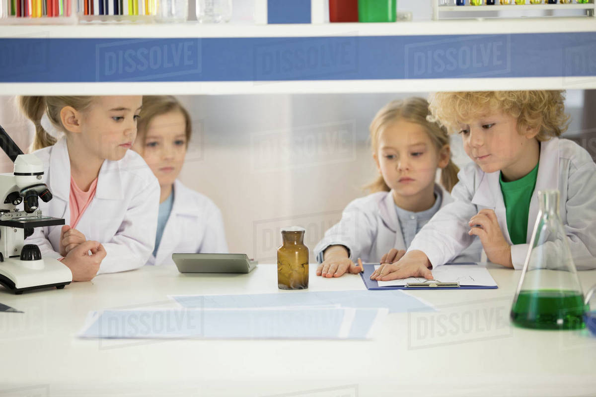 Schoolchildren in lab coats studying together in chemical laboratory ...
