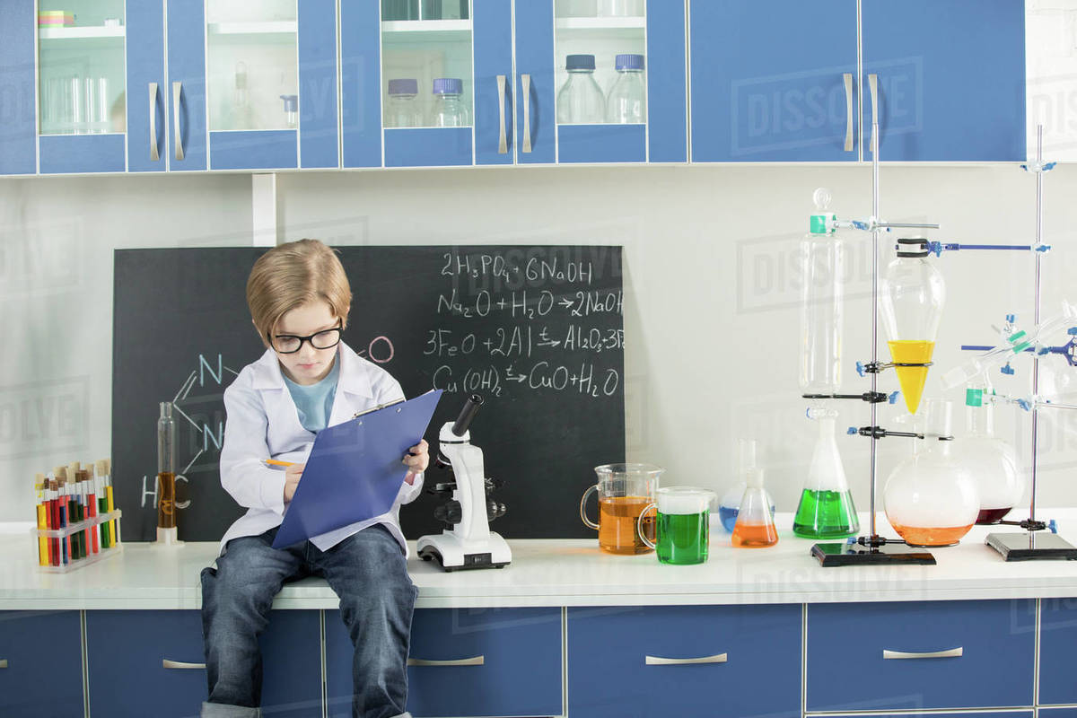 Little boy wearing lab coat making notes in clipboard in science ...