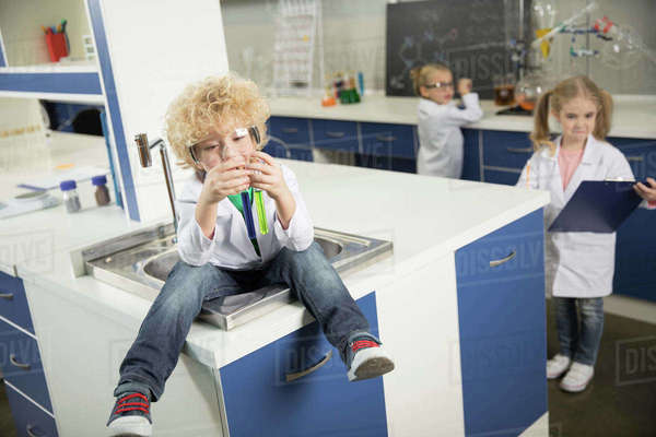 Little boy sitting in sink in science laboratory and holding test tubes ...
