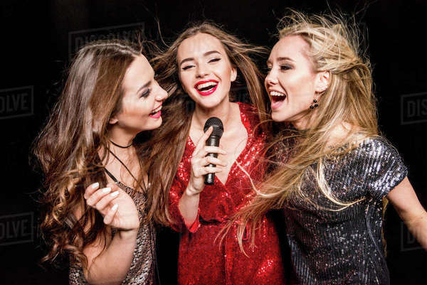 Three gorgeous young women in festive dresses singing karaoke - Royalty ...