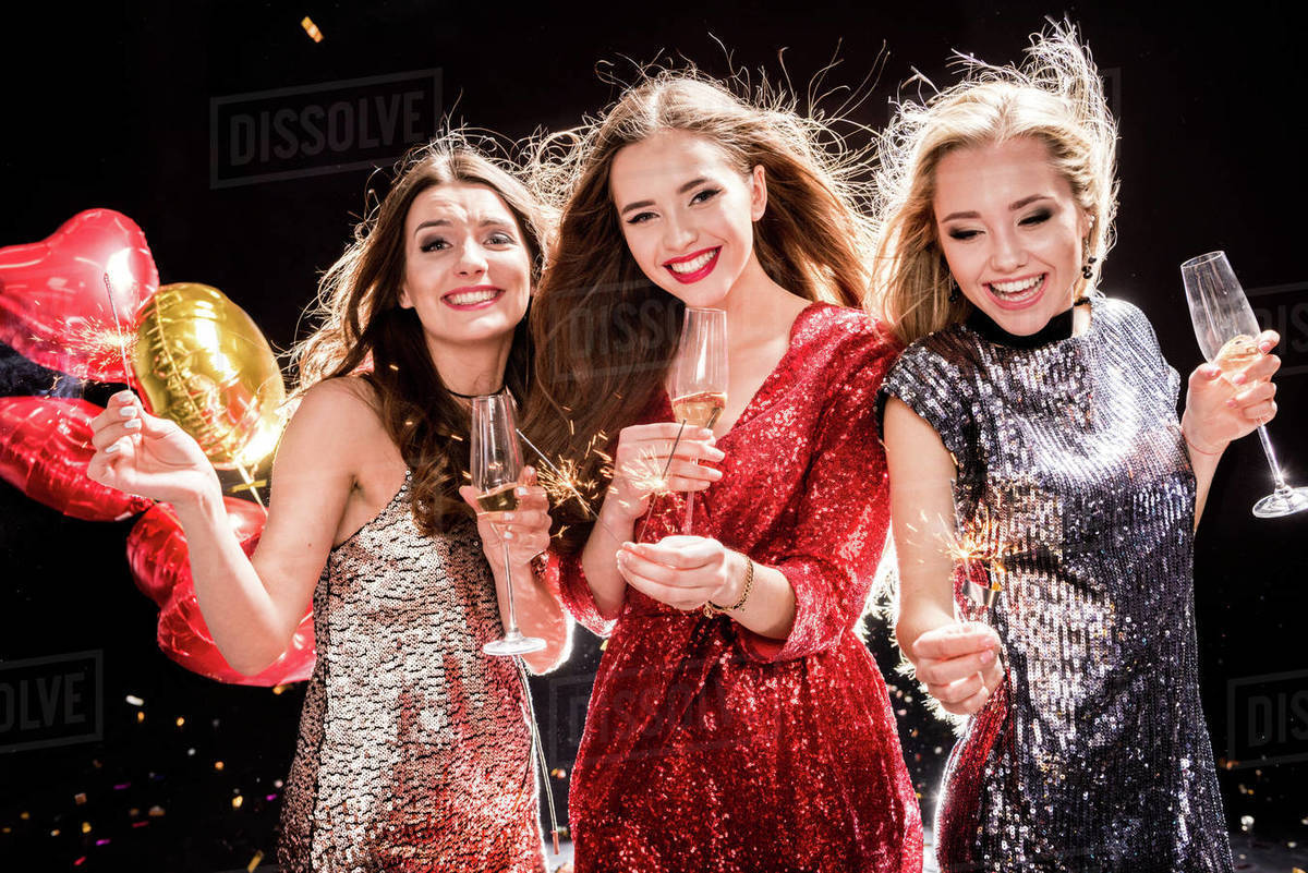 Three happy women in glittering dresses holding glasses of champagne ...