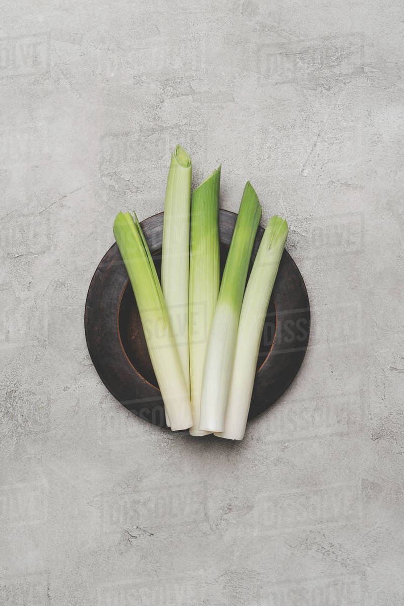 Top view of fresh healthy leeks on plate on grey - Stock Photo - Dissolve