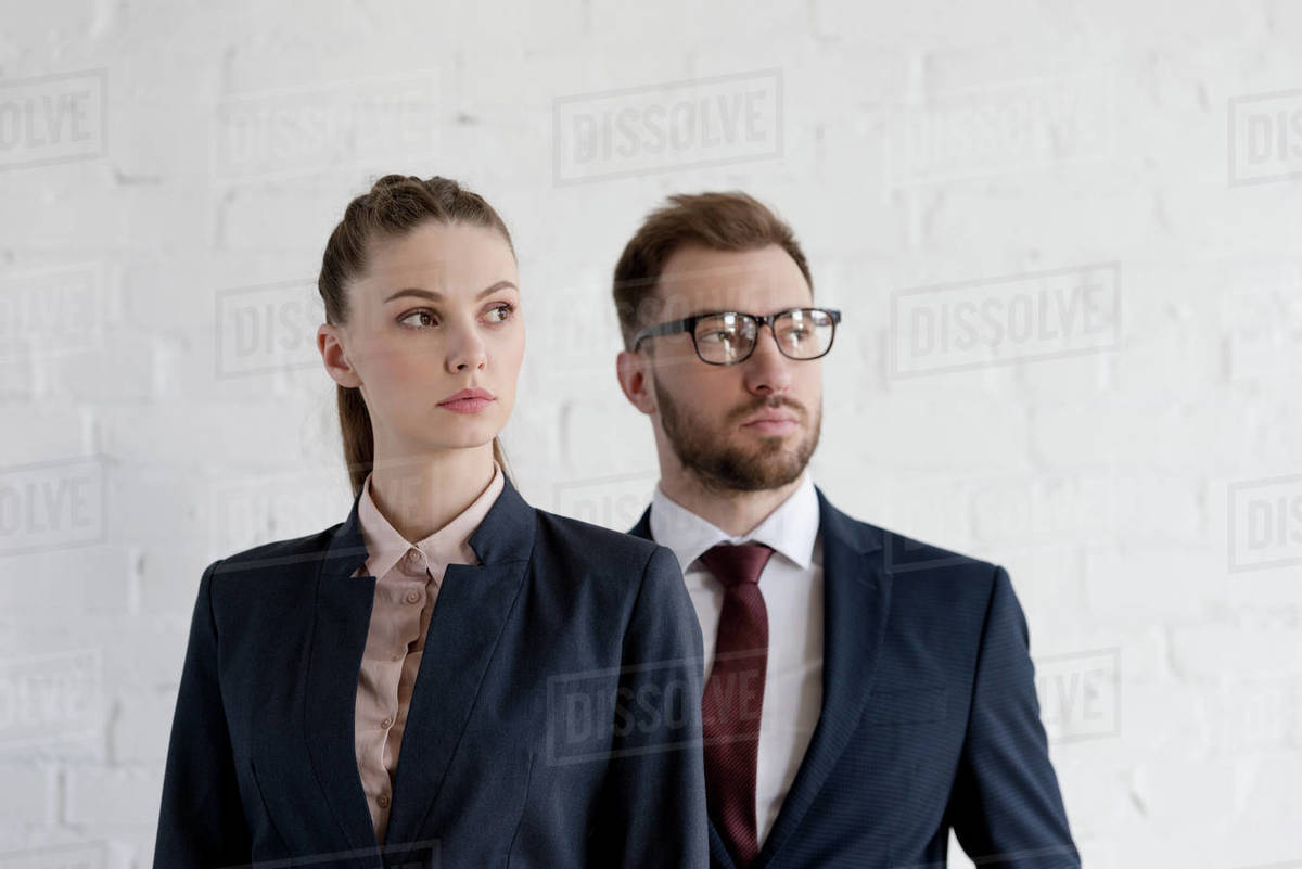 Confident businesspeople in formal wear posing near white wall ...