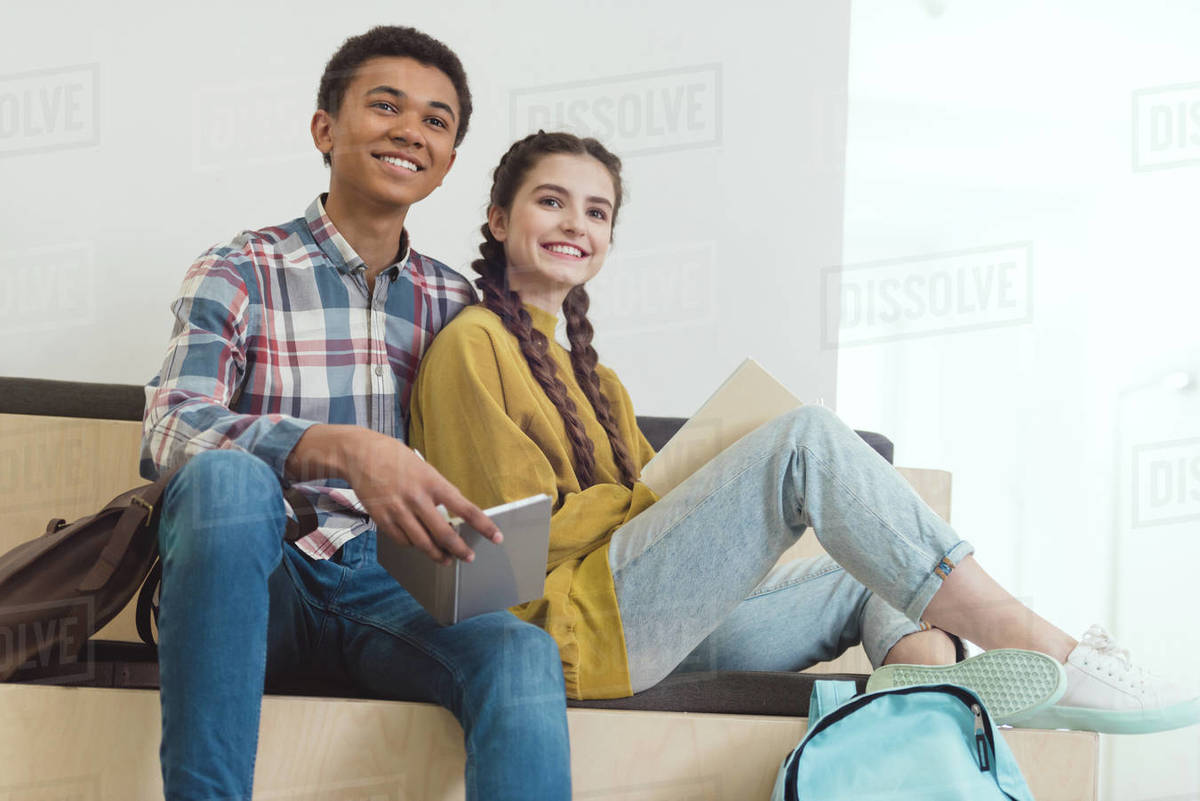 Happy high school students couple doing homework at school corridor ...
