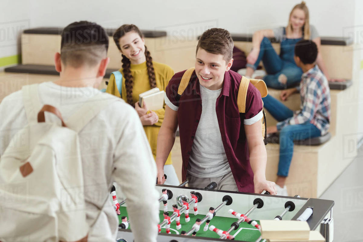 Happy high school students playing table football at school corridor ...