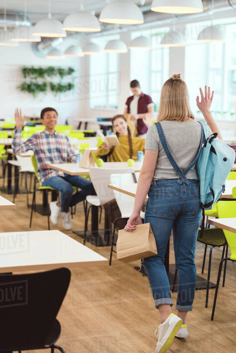 Happy high school students greeting their classmate at school cafeteria ...