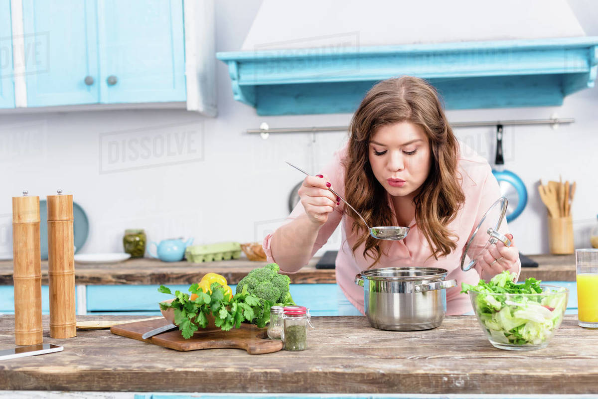 Portrait of young overweight woman cooking soup in kitchen at home ...