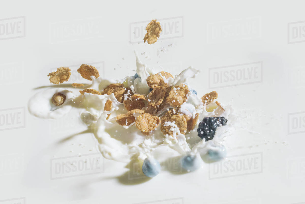 Cereals and berries falling in milk with drops on white background ...