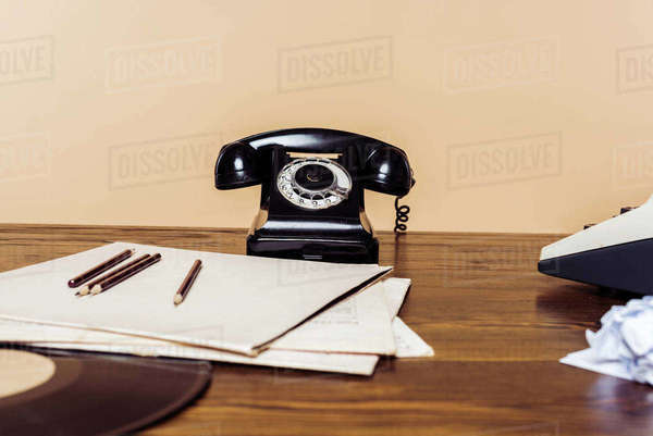 Close-up shot of rotary phone on wooden table with typewriter and vinyl ...