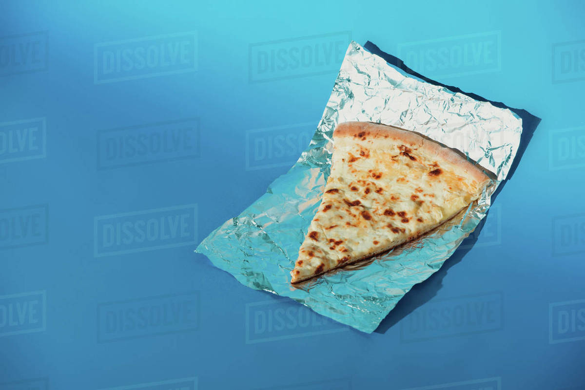 Close up view of piece of Italian pizza on foil on blue background ...