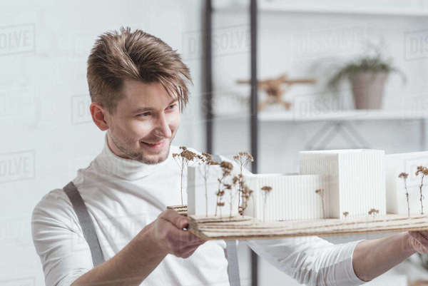 Portrait of smiling architect looking at self made building model in ...