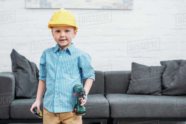 Little boy in safety helmet with toy drill pretending to be workman ...