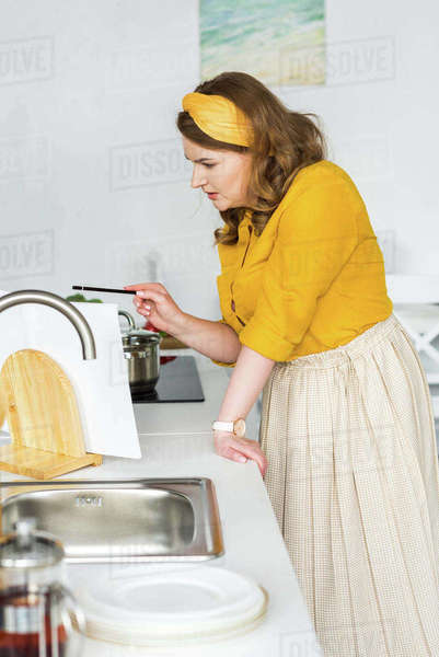 Beautiful woman reading recipe in recipe book in kitchen - Stock Photo ...