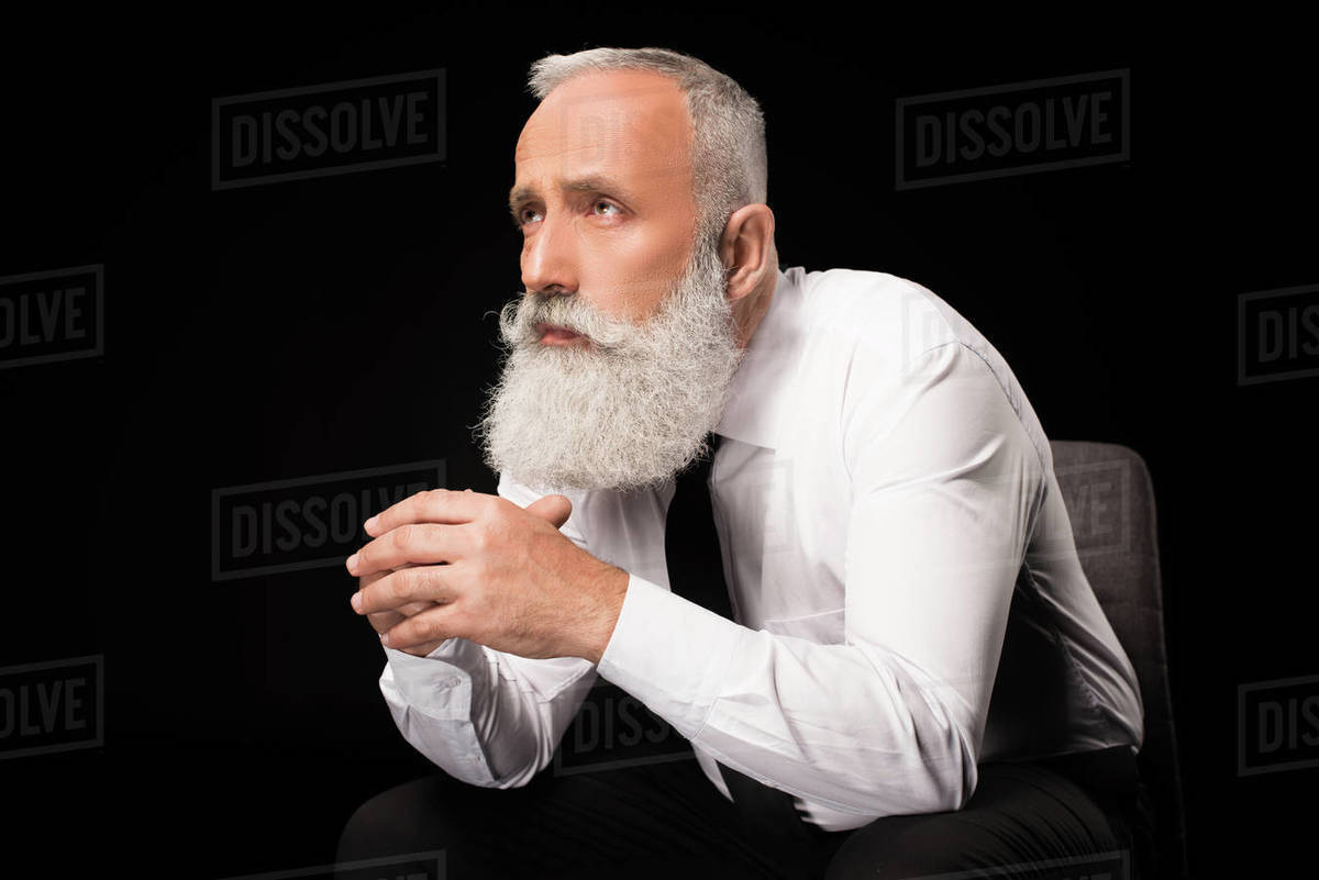 Half-length shot of man in a suit sitting on a chair with his hands ...