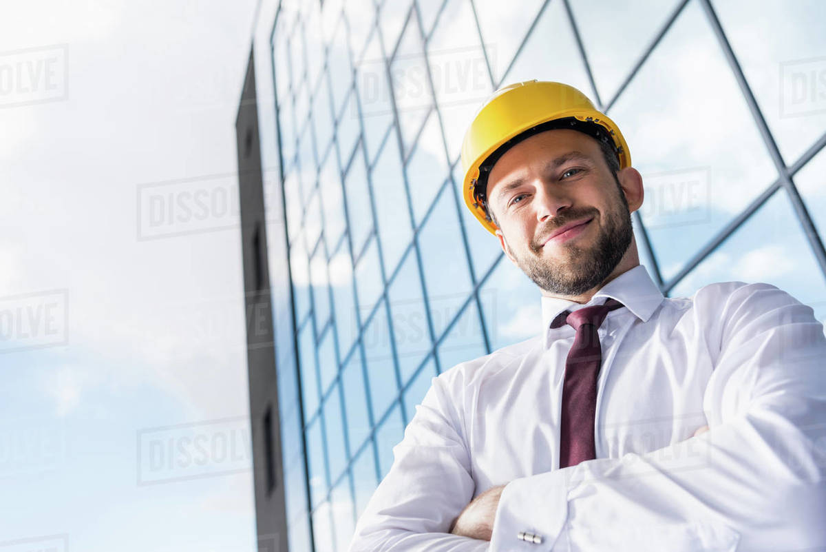 portrait of smiling professional architect in hard hat against building ...