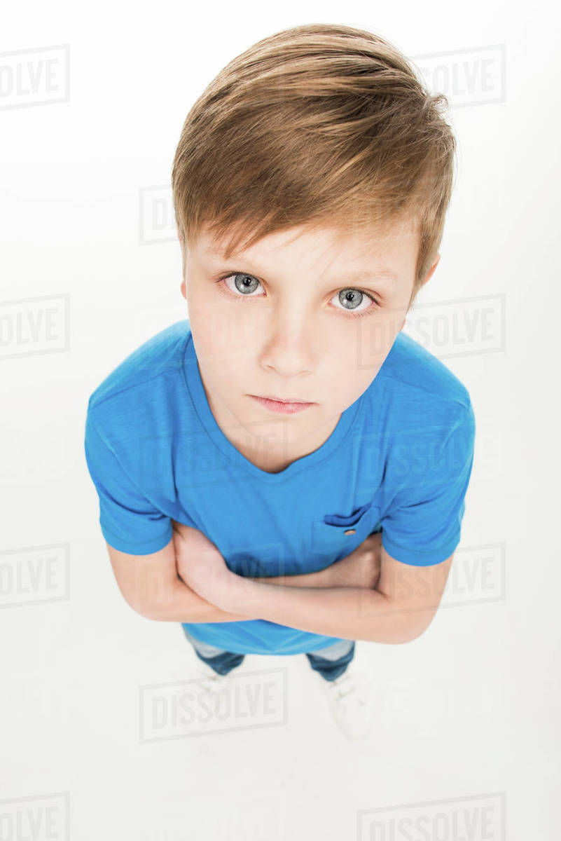 High angle view of serious little boy standing with crossed arms and ...
