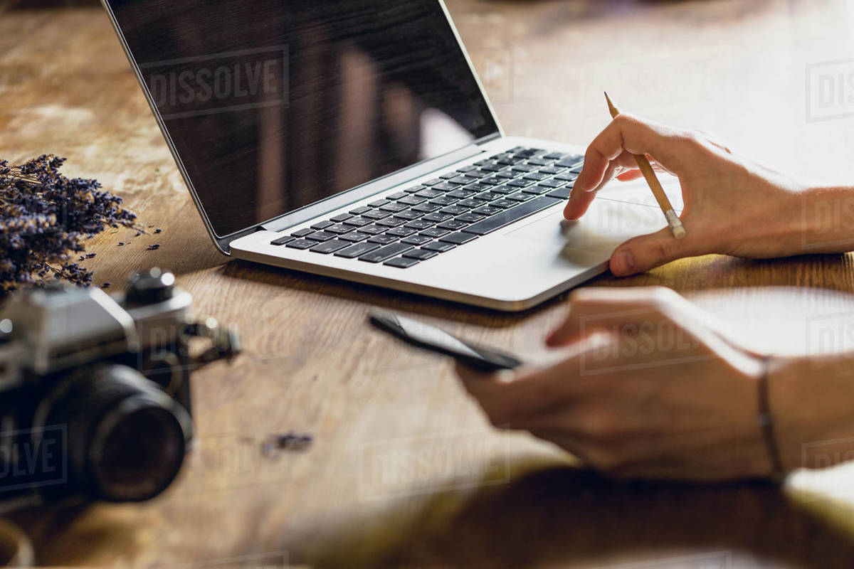 Person using laptop and smartphone at workspace with vintage photo ...