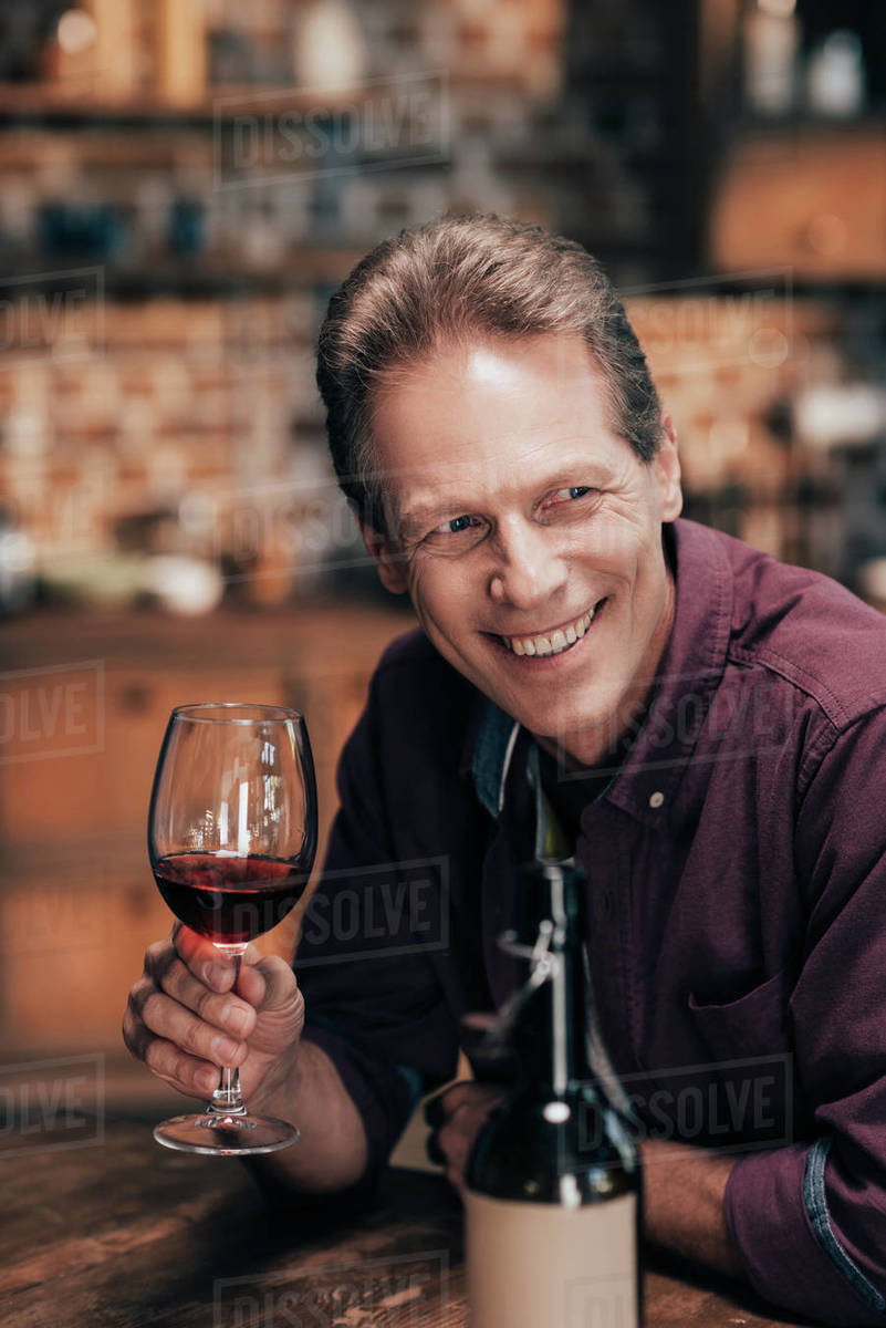 Handsome smiling man holding glass of wine and looking away - Stock ...