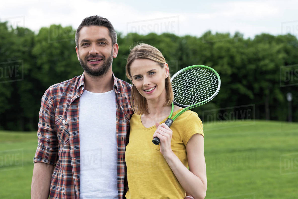 Happy young couple with badminton racquet standing together in park ...