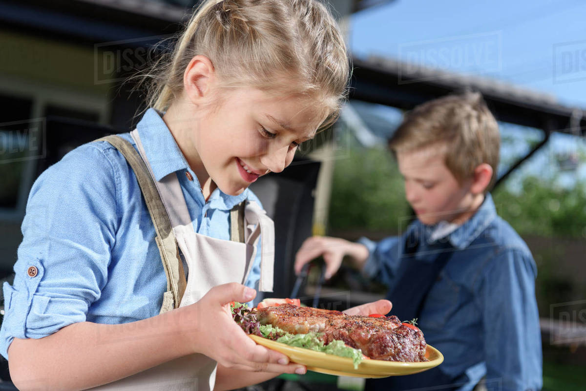 adorable kid girl holding plate with fresh cooked steaks while her ...
