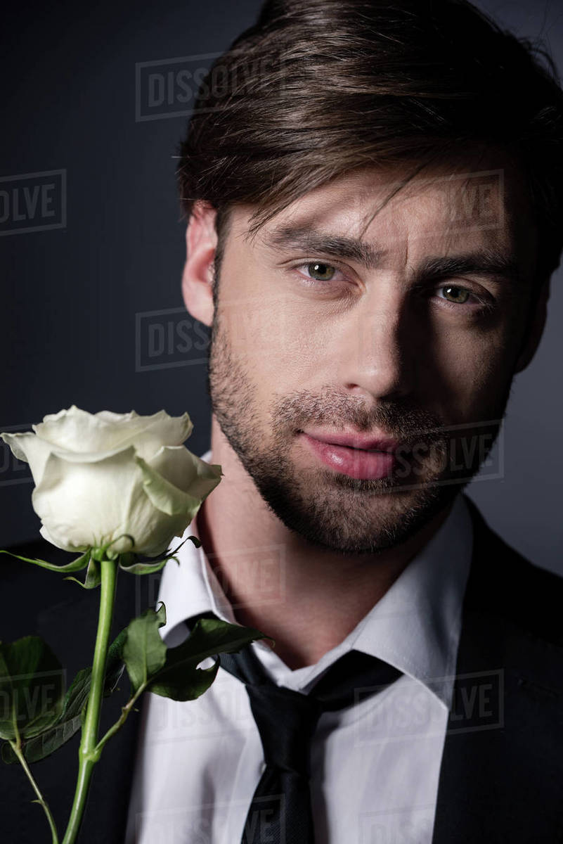 portrait of young man in suit with white rose isolated on black ...