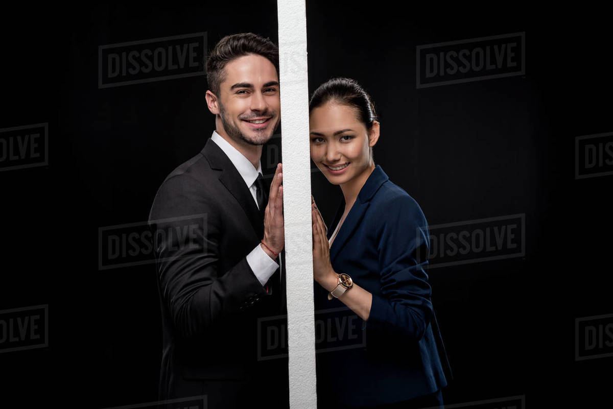 Side view of young smiling couple separated by wall and looking at ...