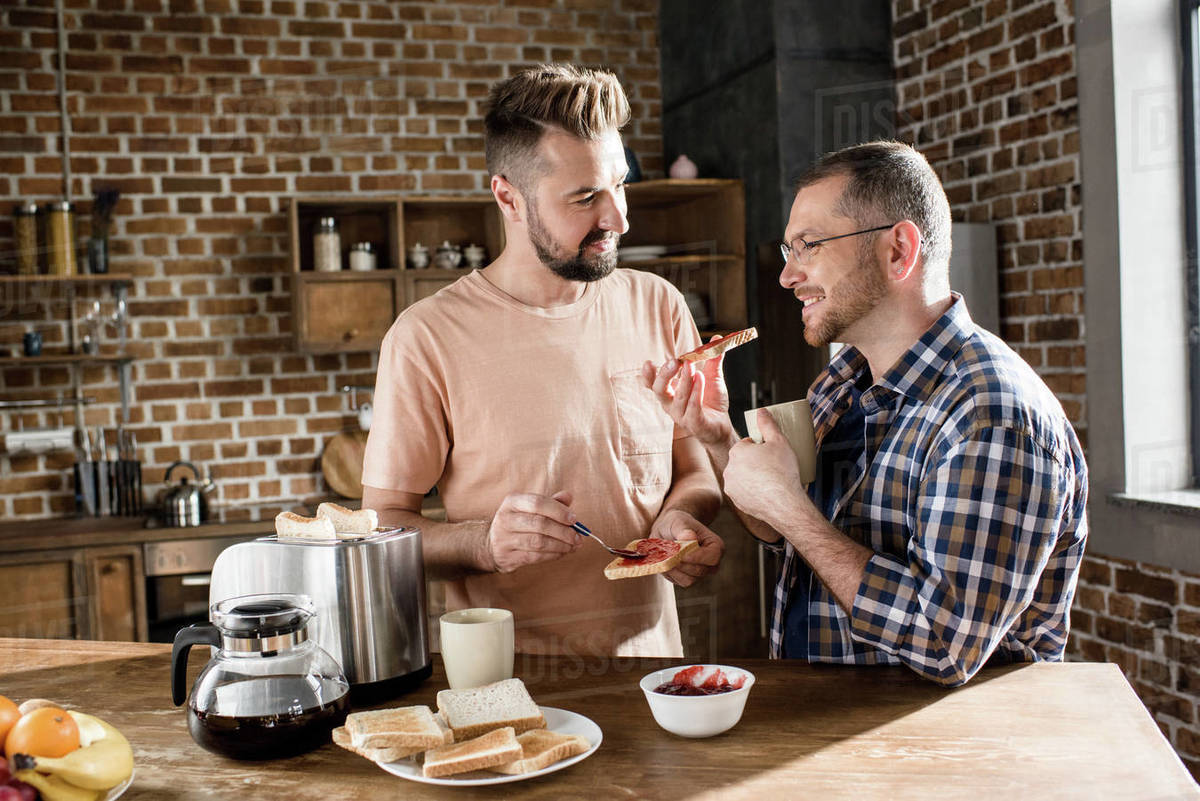 Happy gay couple eating toasts with jam in kitchen at morning - Royalty ...