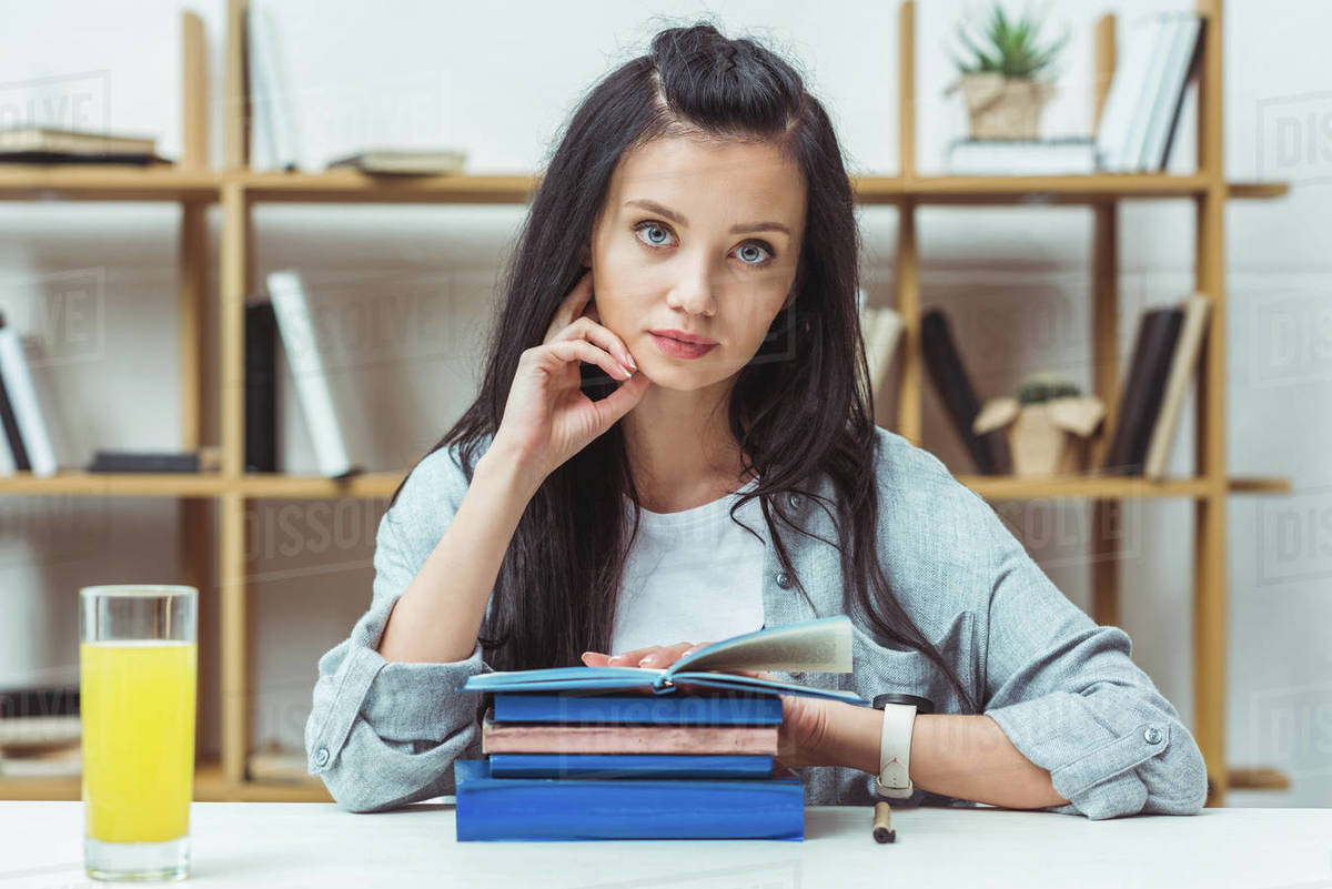 Beautiful young woman studying with books and looking at camera ...
