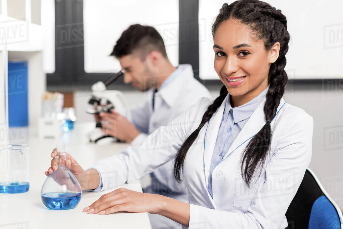 Young scientist in lab coat sitting at table in laboratory with test ...
