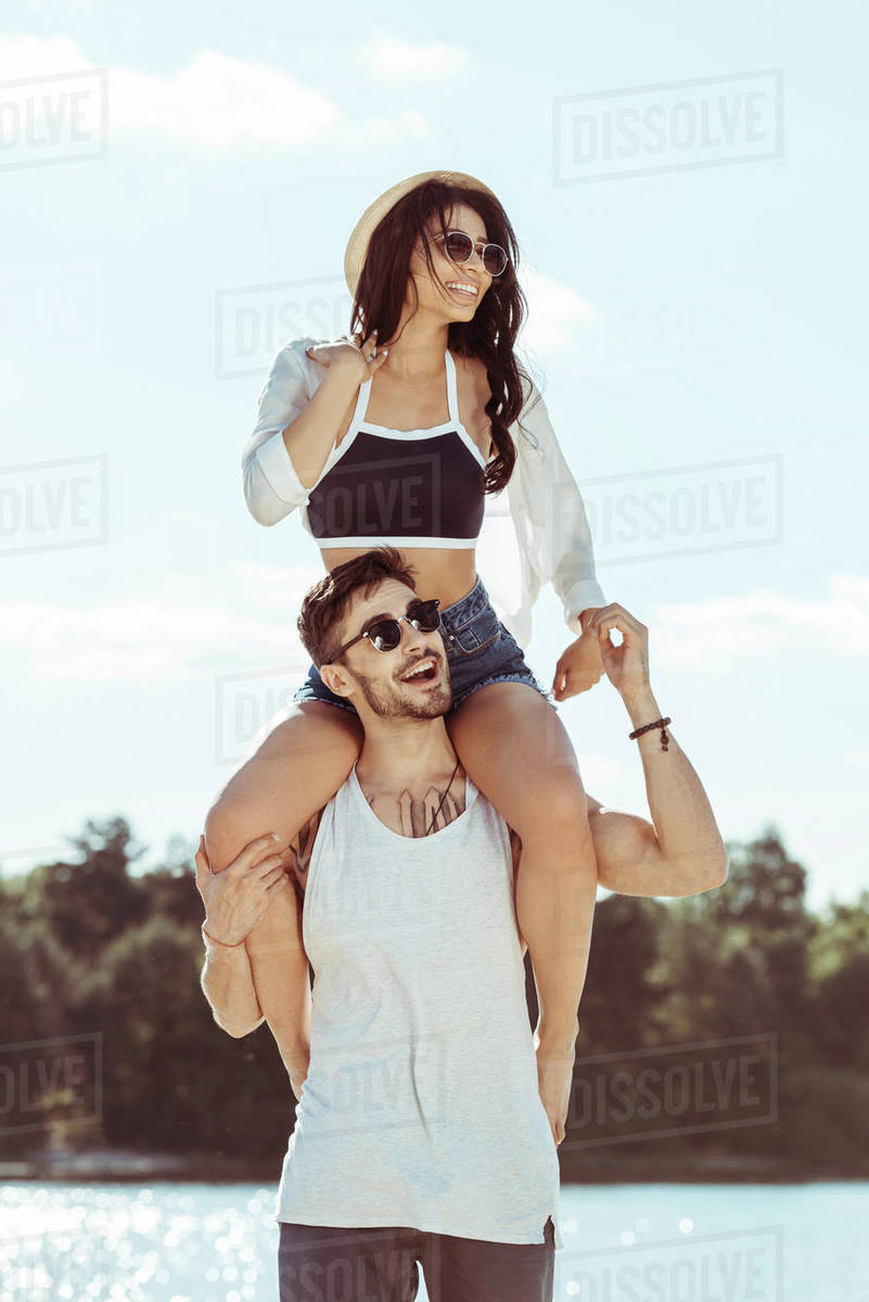 Handsome young man carrying beautiful girl on shoulders at beach ...