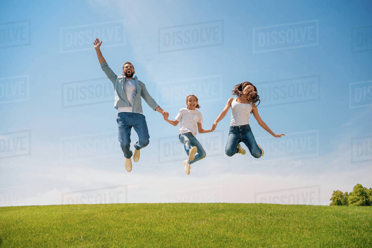 Happy young family with one child holding hands and jumping on meadow ...