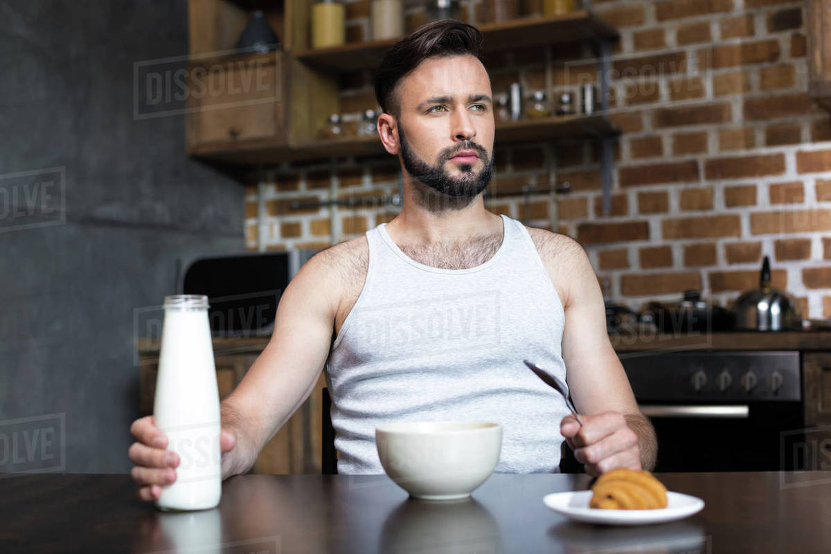 Handsome young man pouring milk from bottle at breakfast - Royalty-free ...